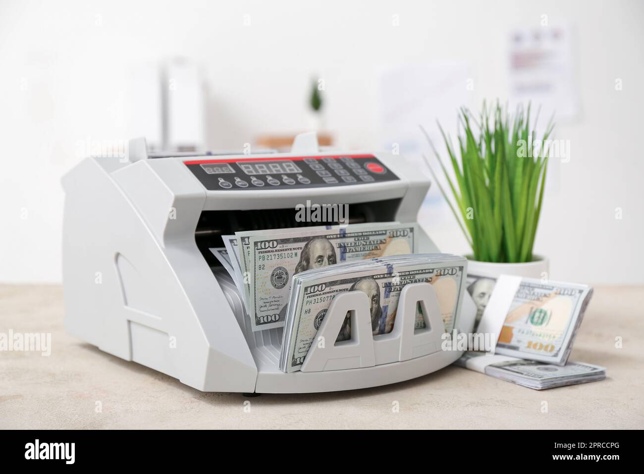 Modern cash counting machine with dollar banknotes and grass on table ...