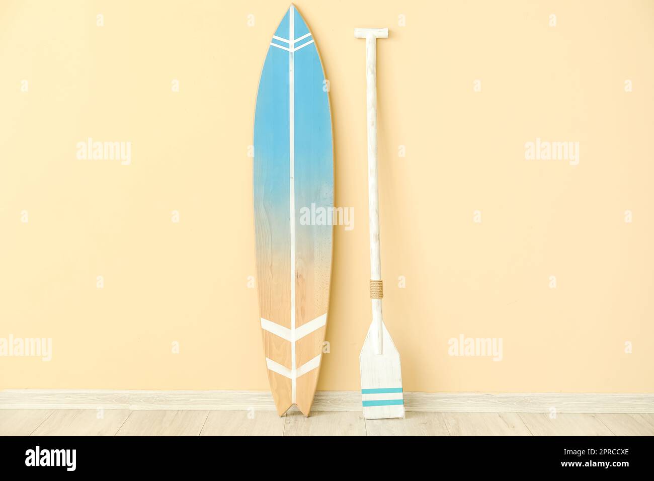 Wooden surfboard with paddle near beige wall Stock Photo - Alamy