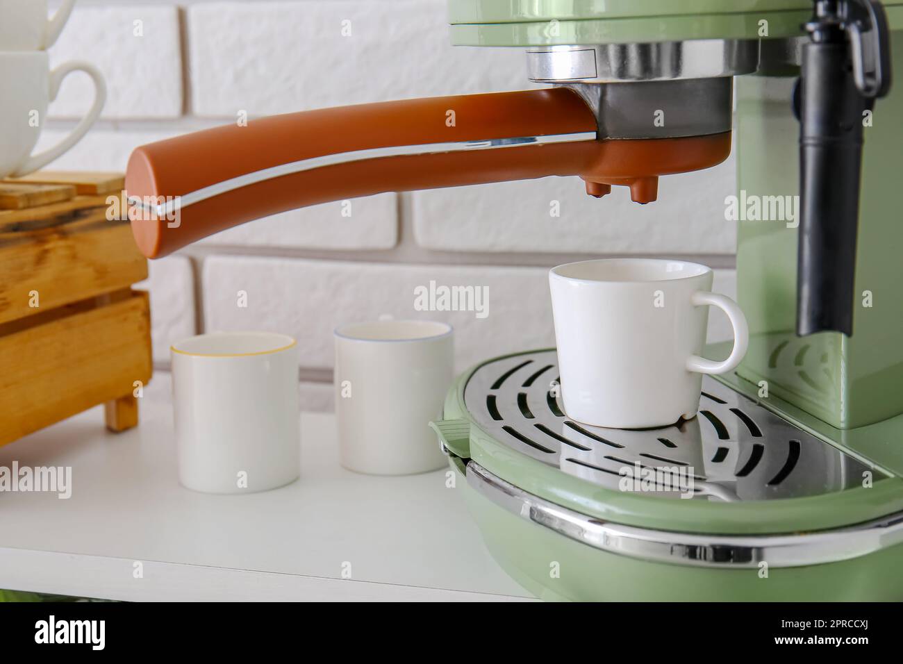 Modern coffee machine with cups on table near white brick wall, closeup ...