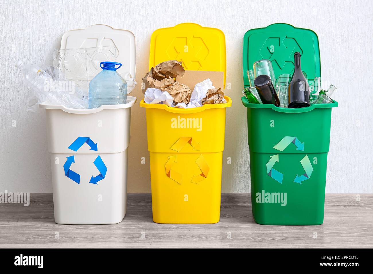 Trash bins with recycling symbol and different garbage near white wall ...