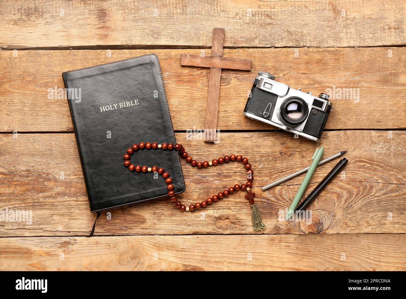 Holy Bible with photo camera, pens, prayer beads and cross on wooden ...