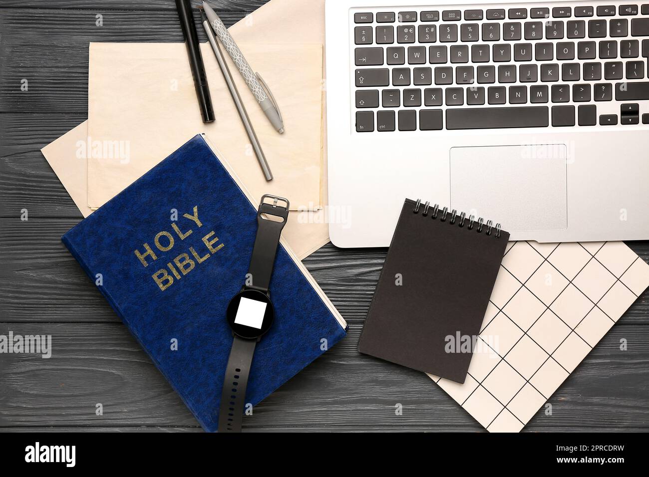 Holy Bible with smartwatch, paper sheets, laptop and notebooks on dark ...