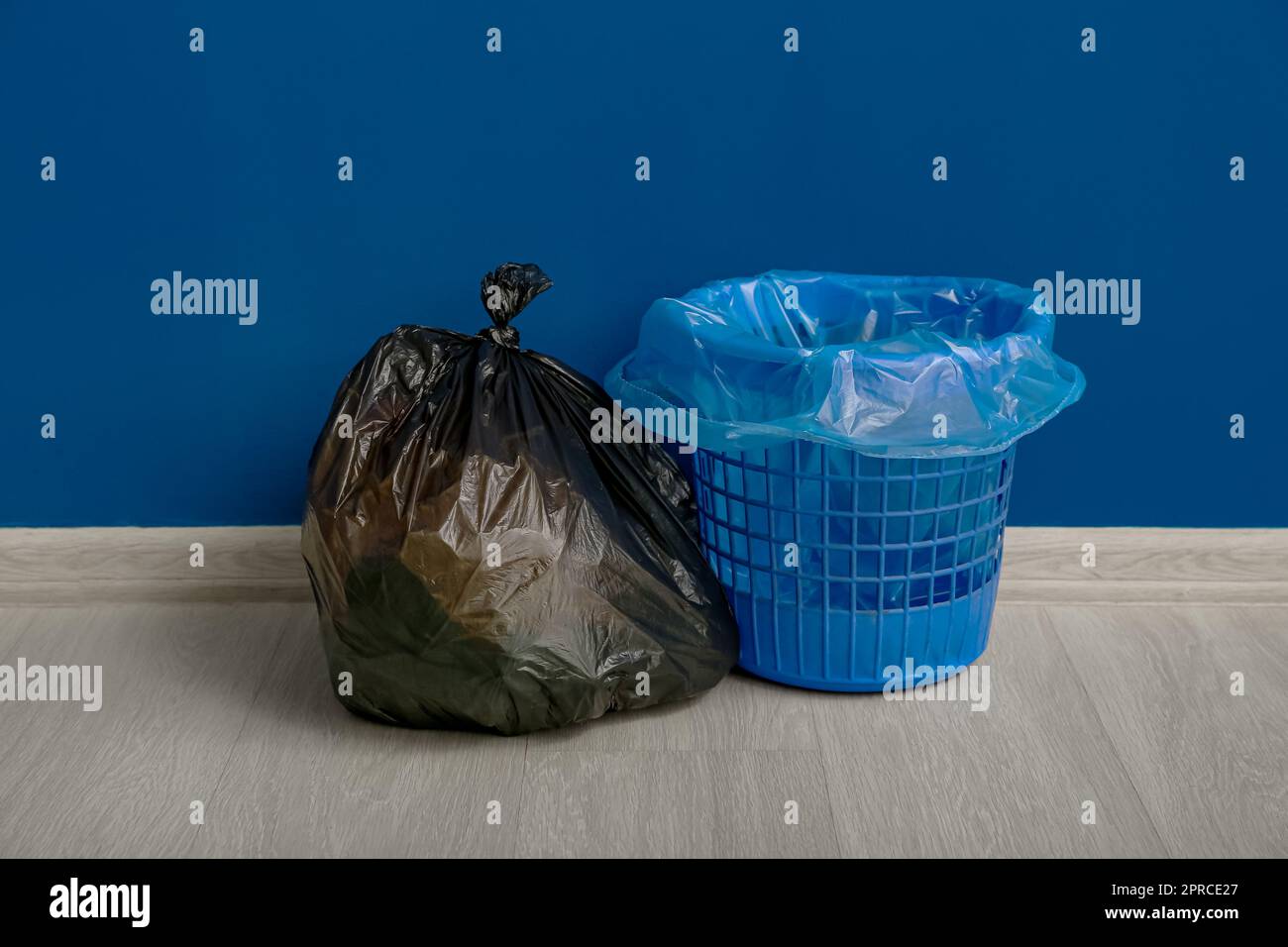 Full garbage bag and empty trash bin near blue wall Stock Photo - Alamy