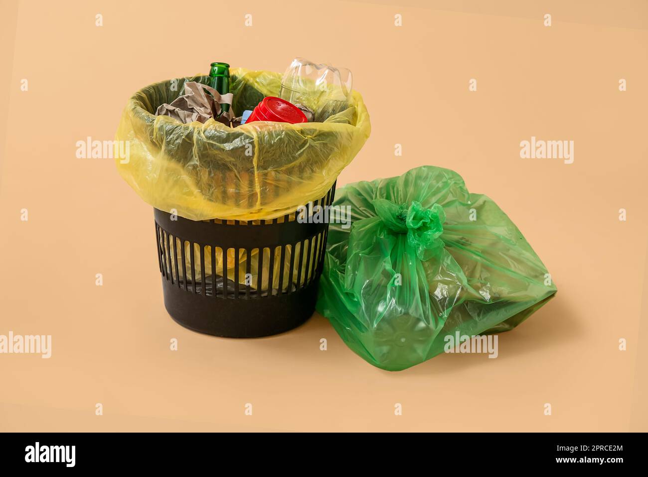Full trash bin and garbage bag on beige background Stock Photo - Alamy