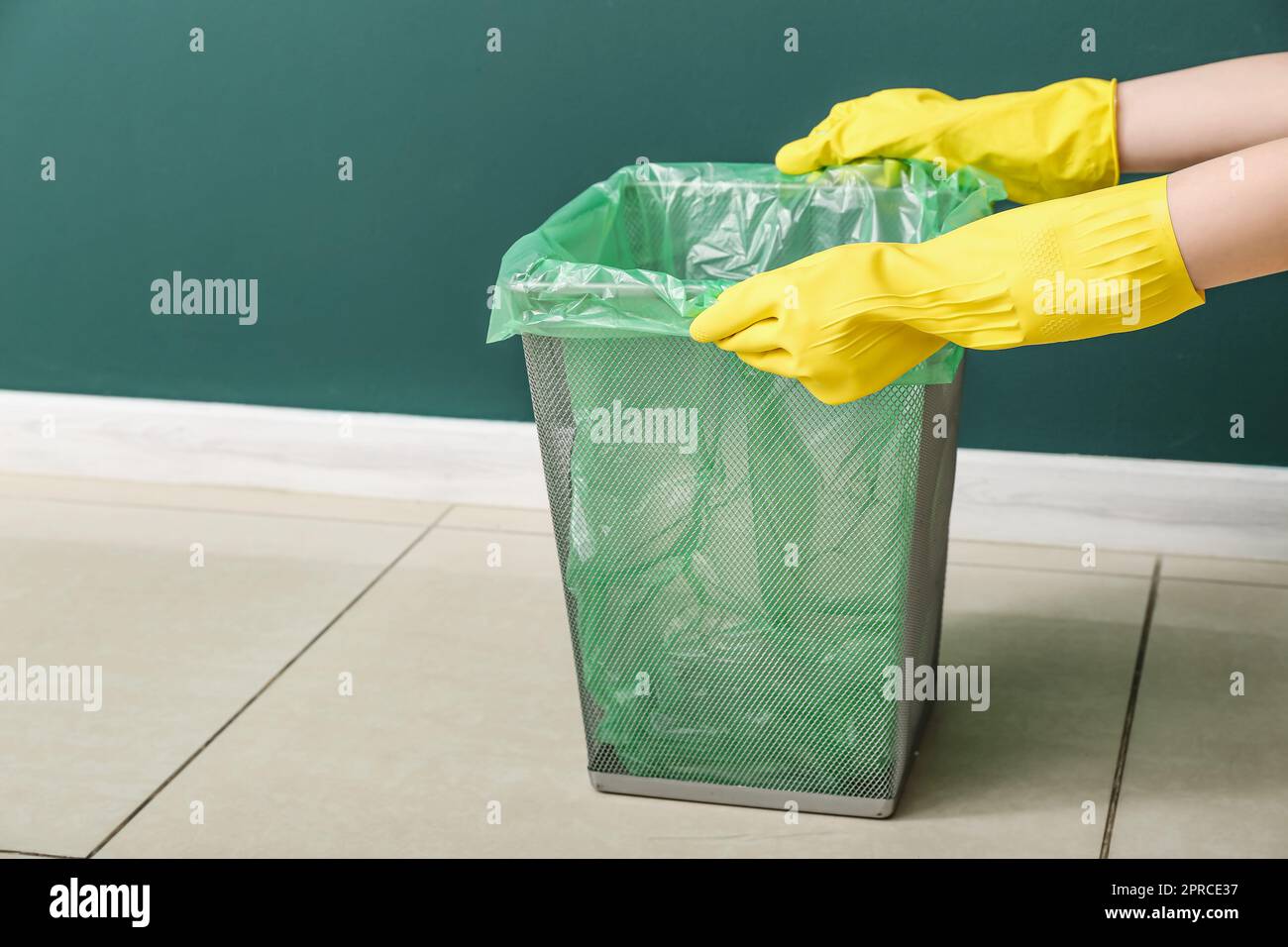 Female hands in rubber gloves putting garbage bag into trash bin near ...