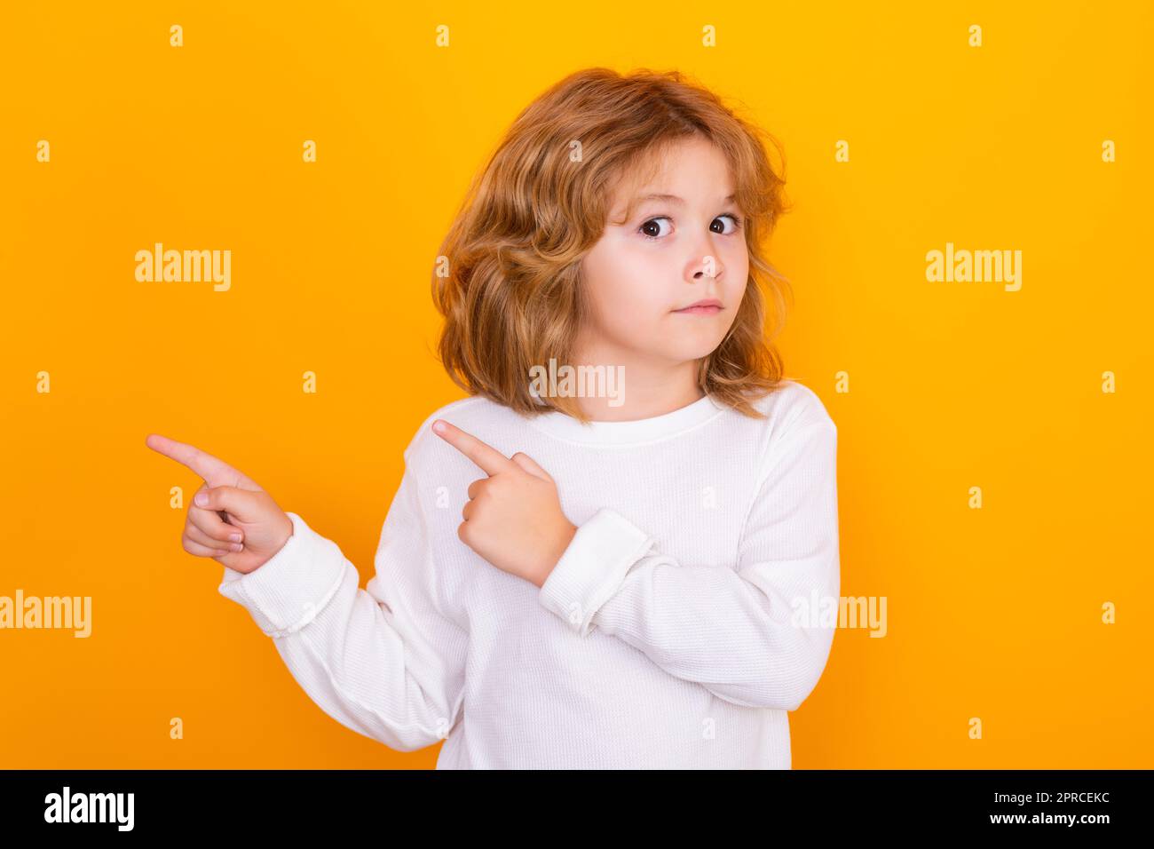 Surprised kid boy pointing finger on yellow isolated studio background ...
