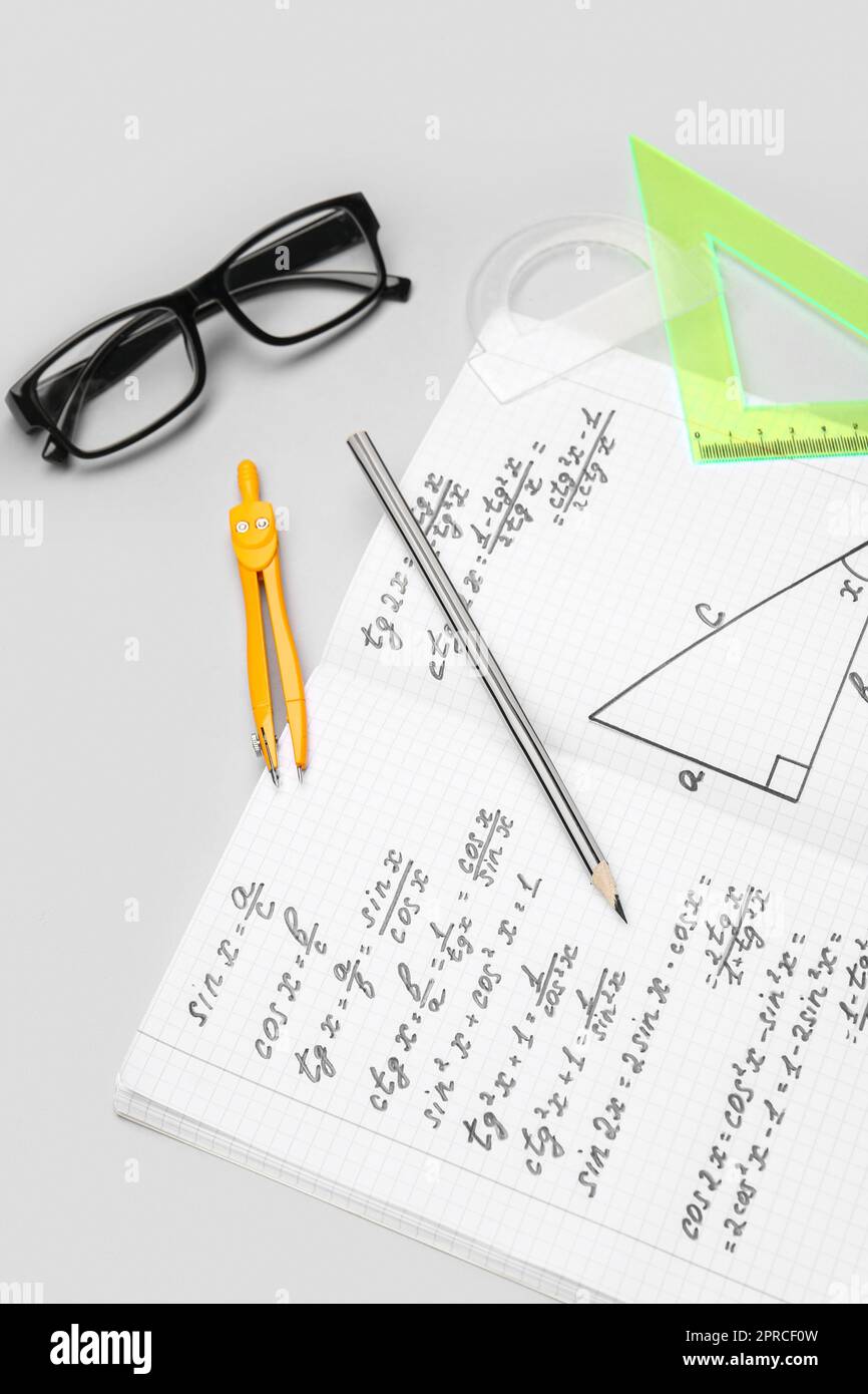 Copybook with maths formulas, glasses and stationery on grey background ...