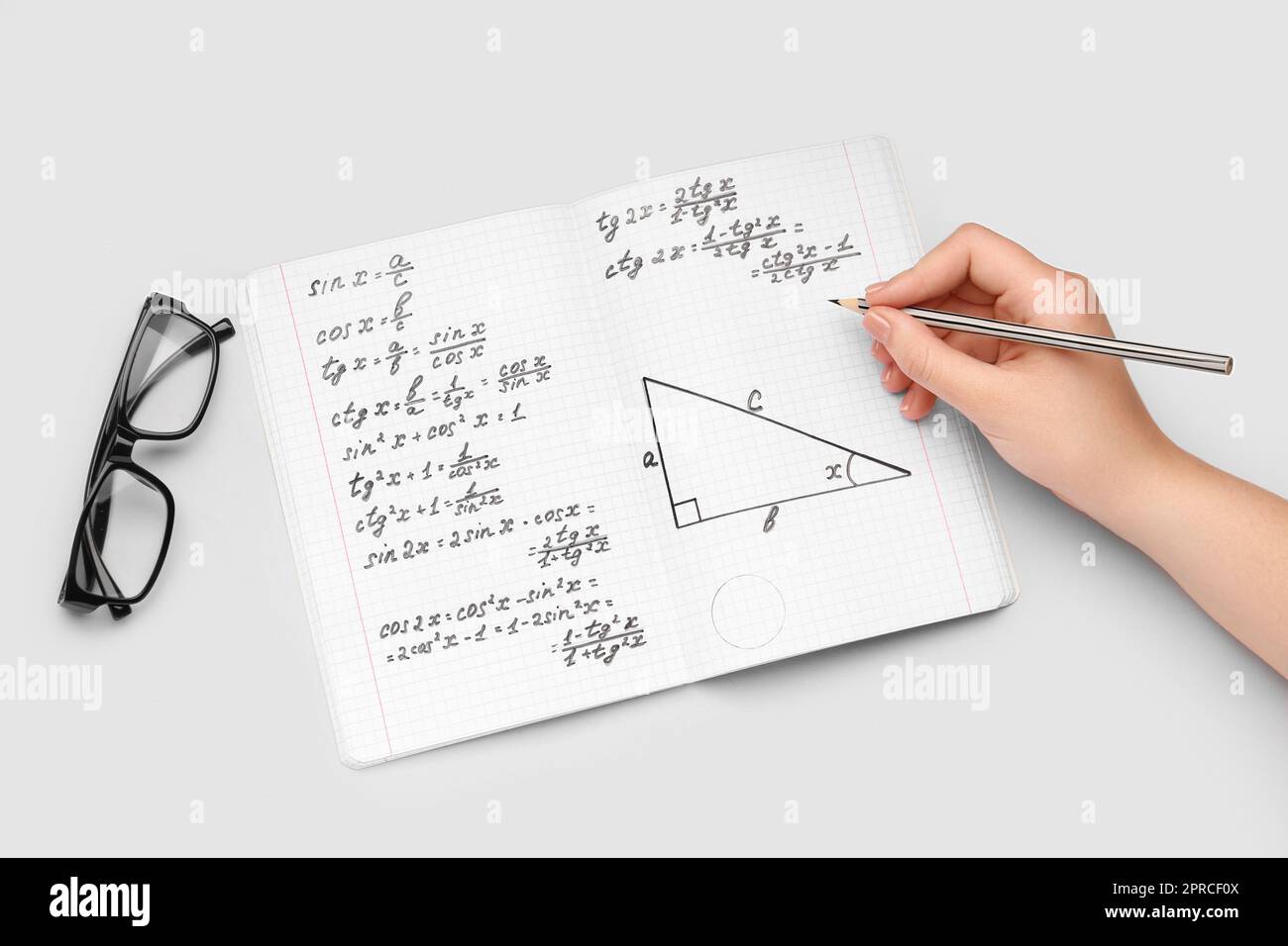 Woman writing maths formulas in copybook with pencil on grey background ...