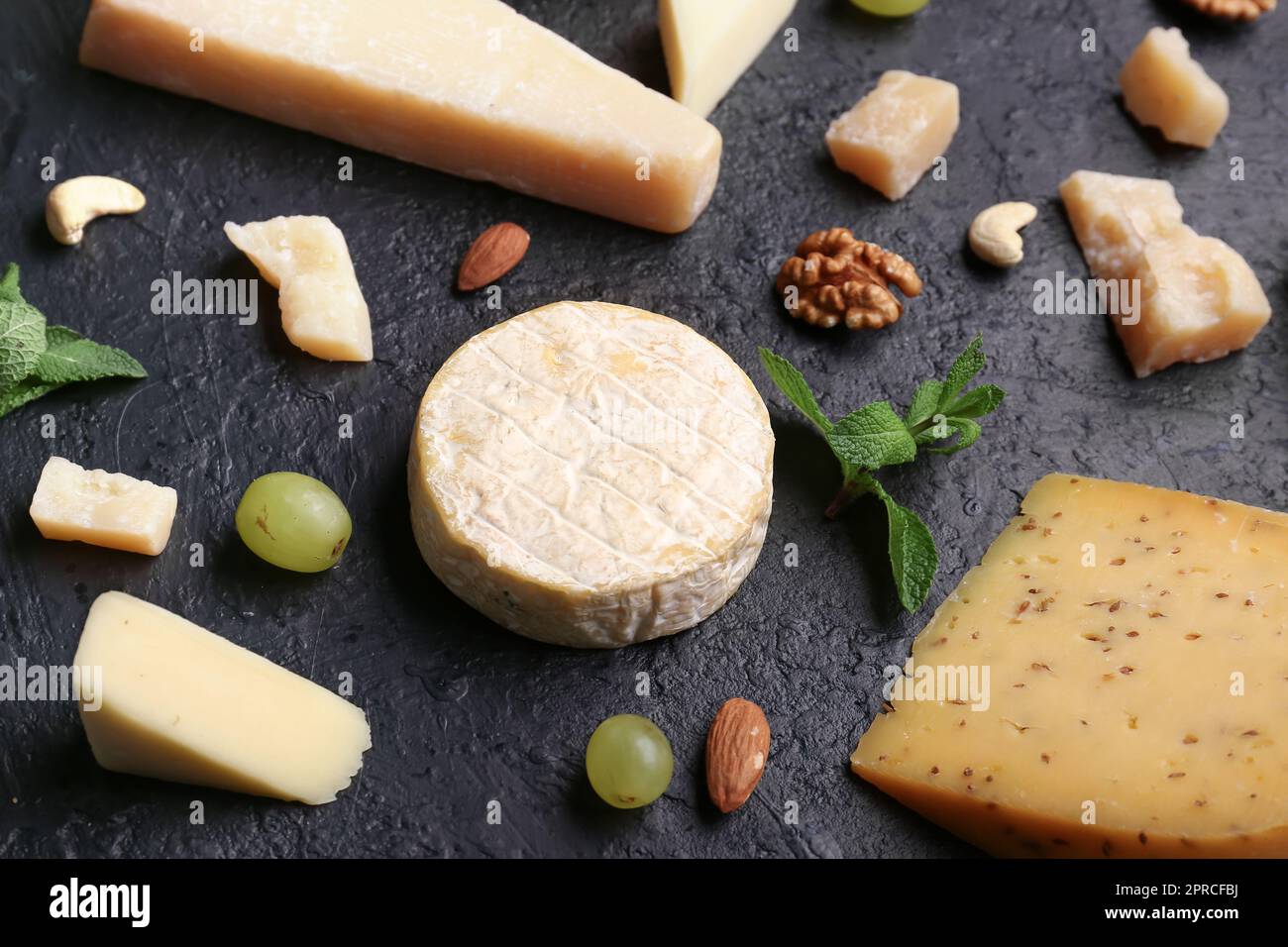 Different types of tasty cheese, grapes and nuts on dark background ...