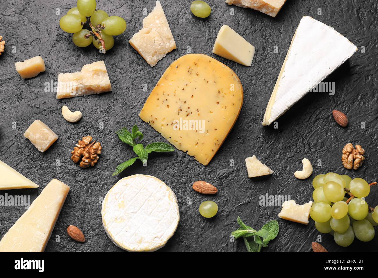 Different types of tasty cheese, grapes and nuts on dark background ...