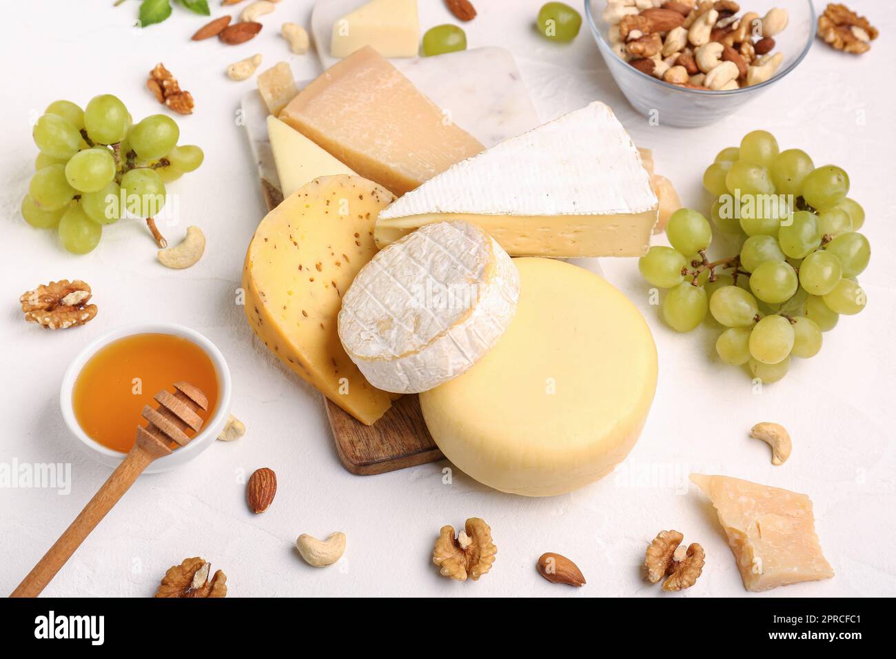 Board with different types of tasty cheese, grapes and honey on light ...