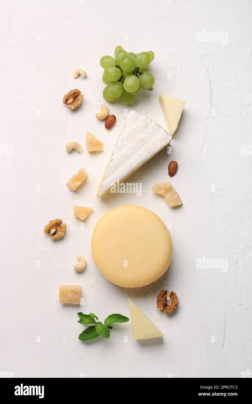 Different types of tasty cheese, nuts and grapes on light background ...
