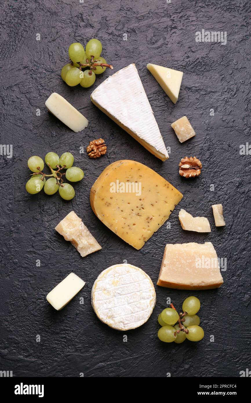 Different types of tasty cheese, nuts and grapes on dark background ...
