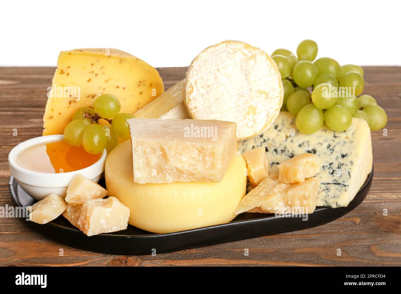 Tray with different types of tasty cheese, honey and grapes on table ...