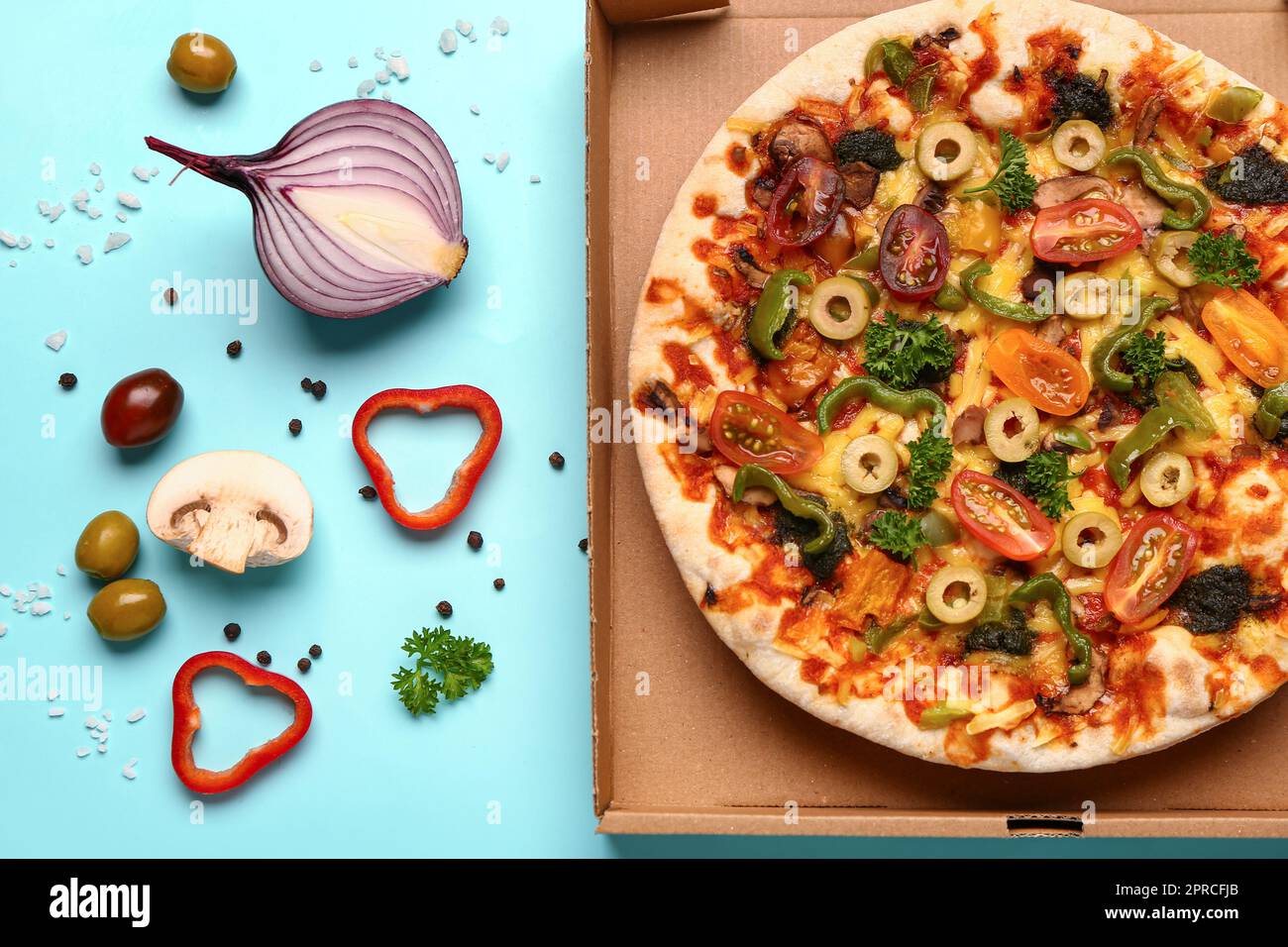 Cardboard box of vegetable pizza with ingredients and cutter on blue ...