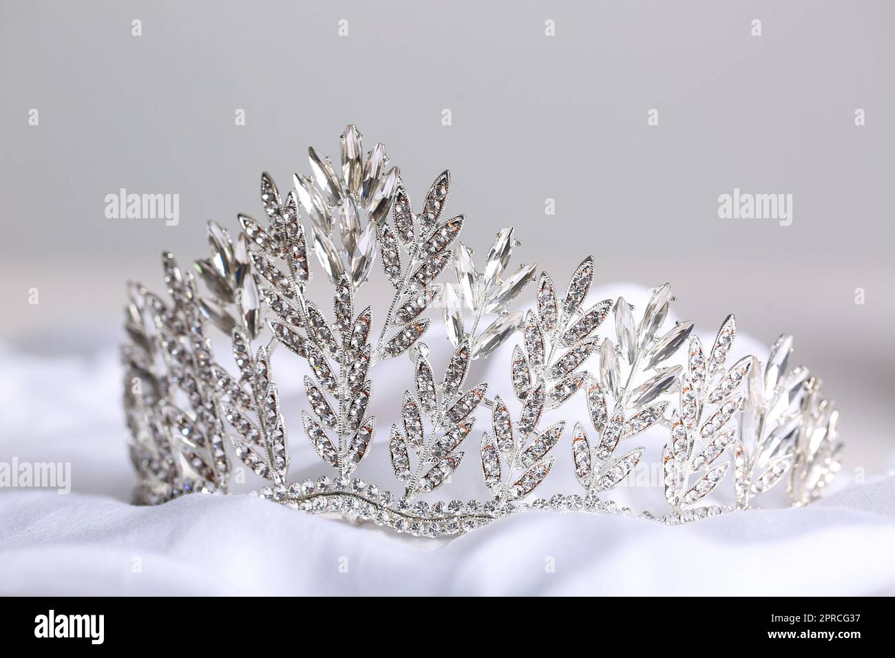 Beautiful tiara on white prom dress against grey background, closeup ...