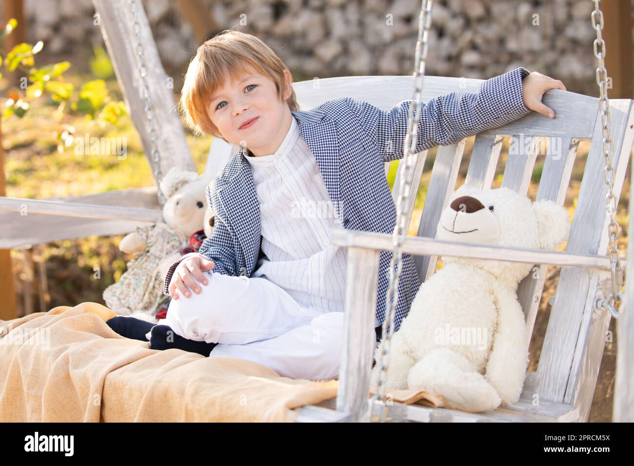 Kid sit on swing bench with toys teddy bear outdoor. Lifestyle closeup ...