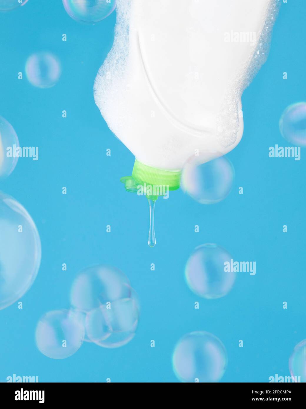A drop of dishwashing gel flows out of a bottle on a blue background ...
