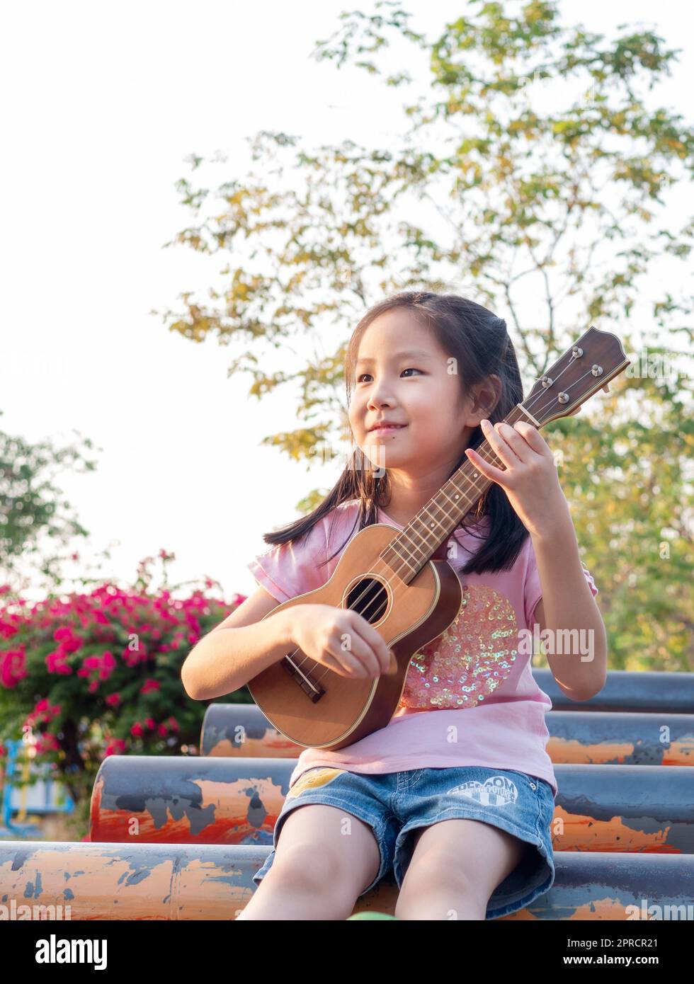 Little asian child girl play the ukulele, in the garden on the Steel ...