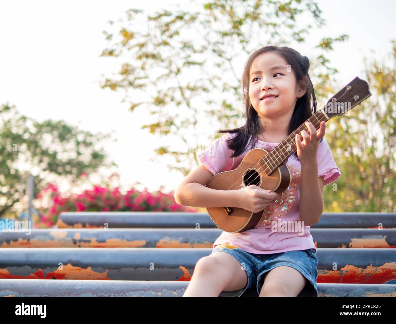 Little asian child girl play the ukulele, in the garden on the Steel ...