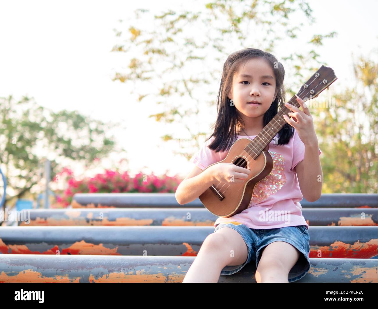 Little asian child girl play the ukulele, in the garden on the Steel ...