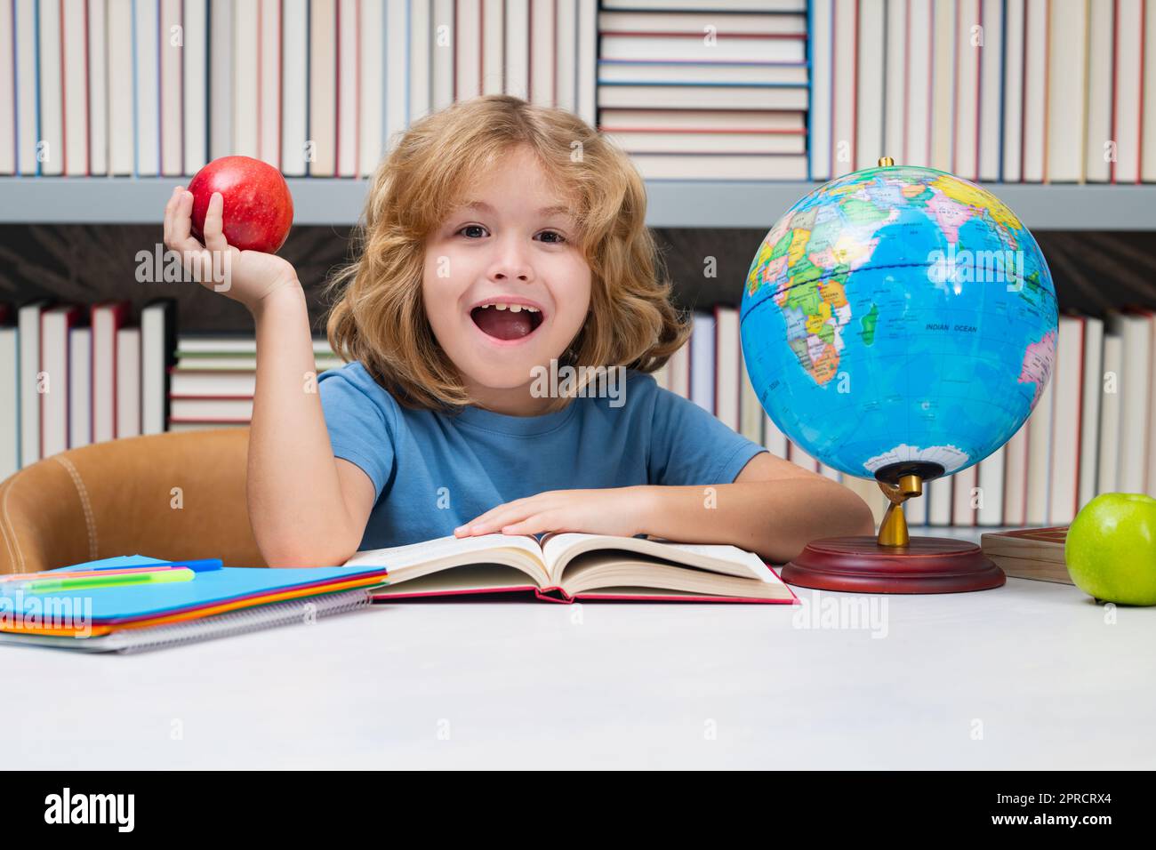Excited pupil. School boy with books and apple in library. School child ...