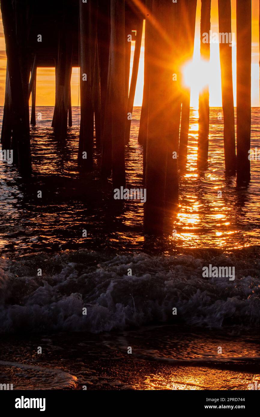 A vertical of sunrise seen through pier pillars over the calm ocean ...