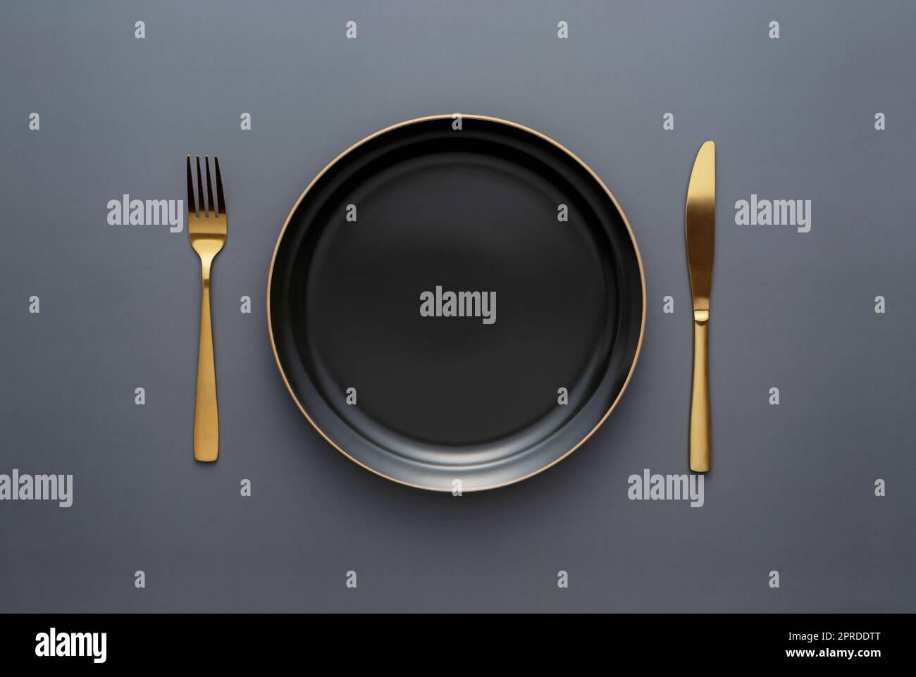 Gold knives and forks on a black background, empty black plate ...