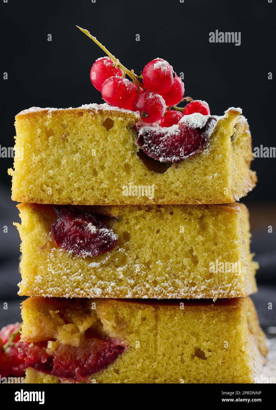 A stack of square slices of baked plum biscuit cake, sprinkled with ...