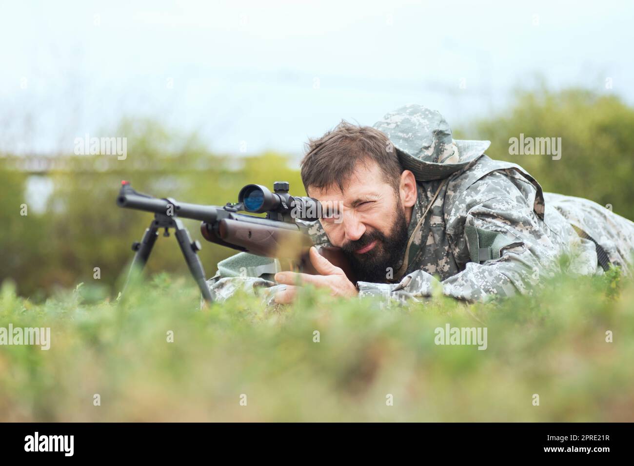 The hunter is aiming and shooting with sniper on shotgun, lying down on ...