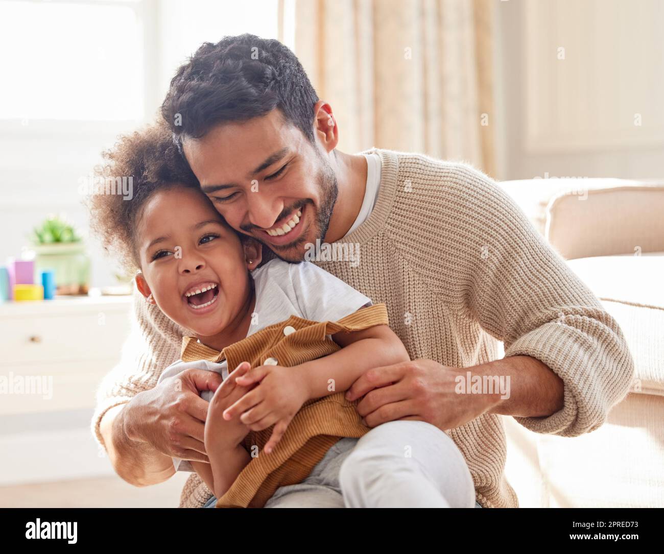 Cheerful young hispanic father tickling his daughter, playing with her. Excited parent bonding ...