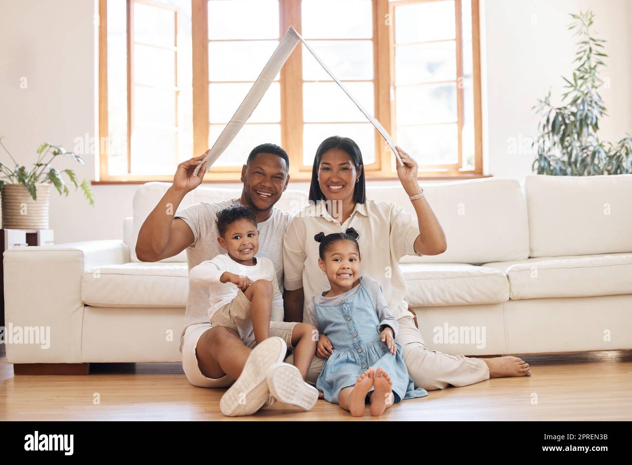 Cheerful parents with two kids smiling and keeping roof mockup over ...