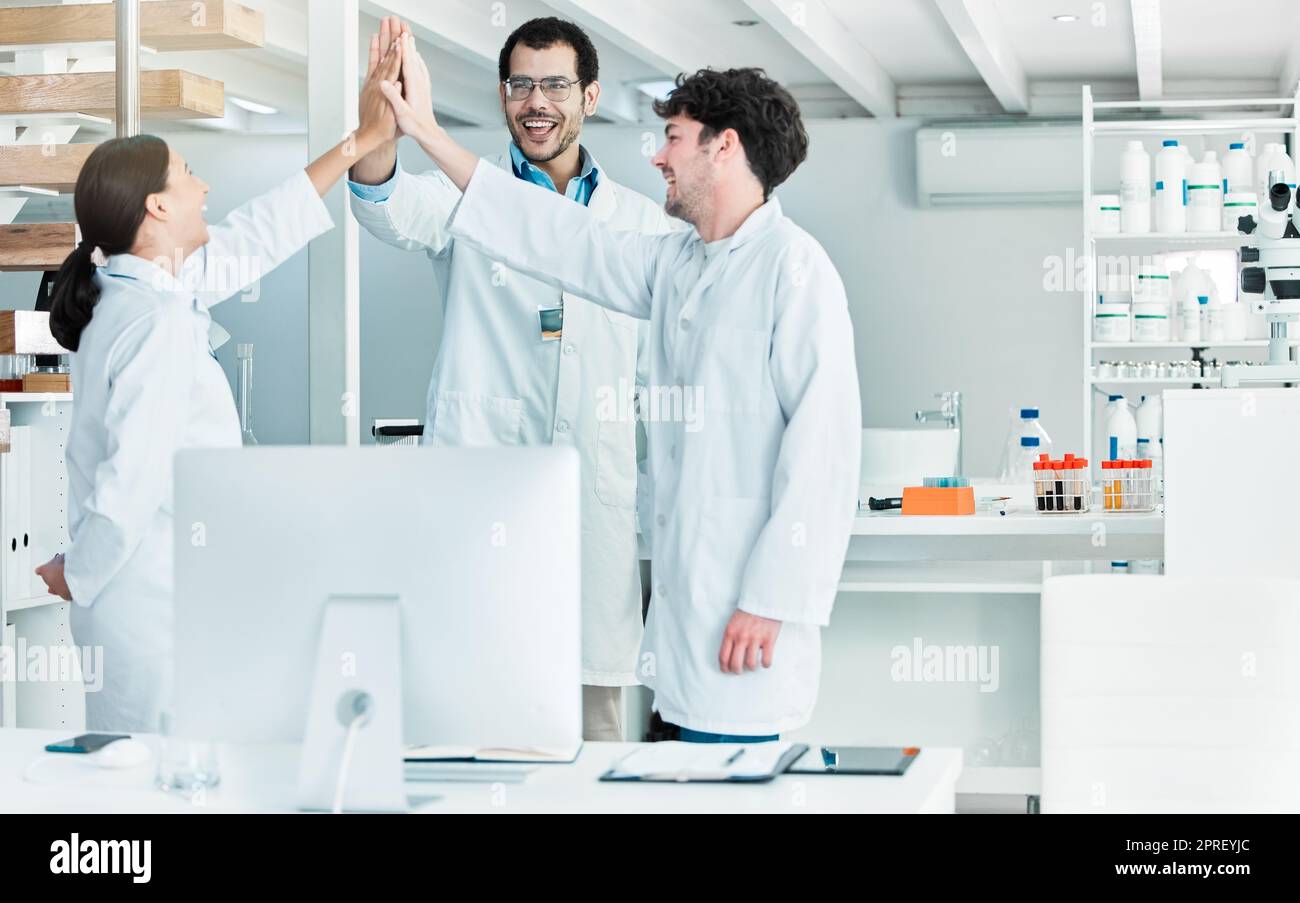 Thrilled by their teams discovery. a group of young scientists giving each other a high five in ...