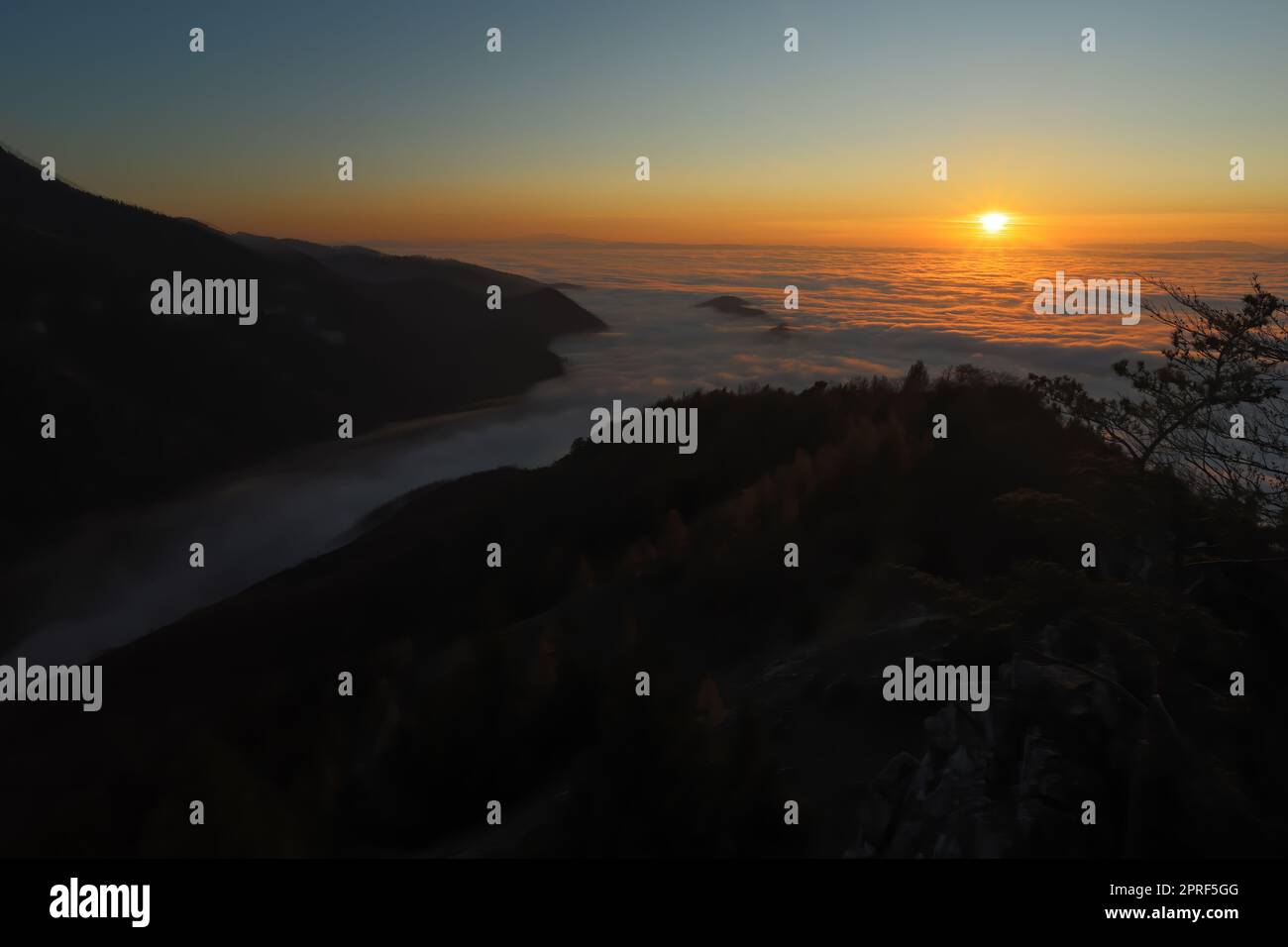 Sun rising above low clouds in mountain with dark hills in background ...