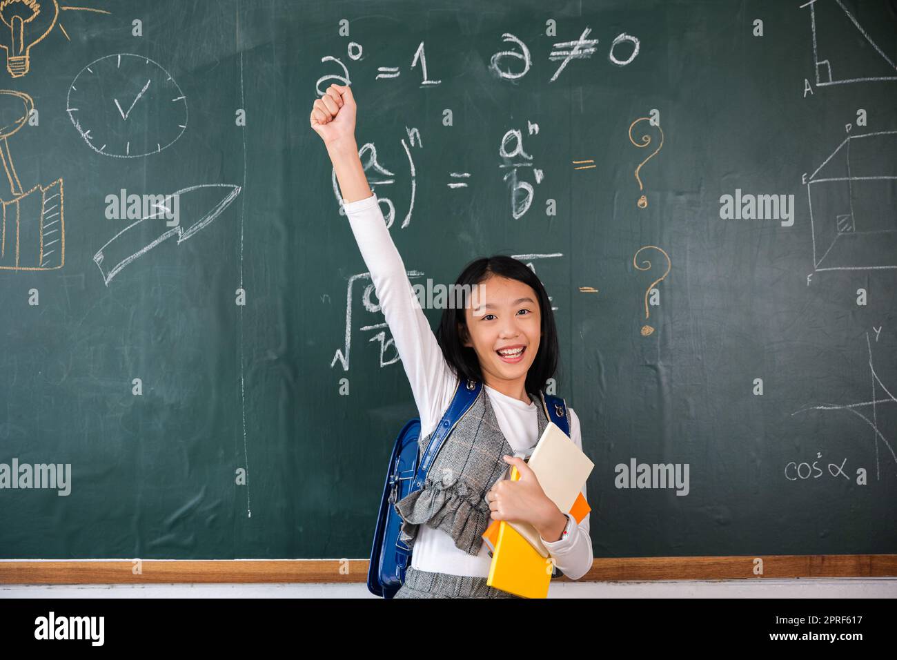 Asian school girl in uniform on classroom raised arms to successful ...