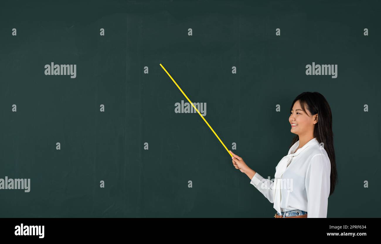Asian female teacher smiling with wooden stick pointing to blackboard ...