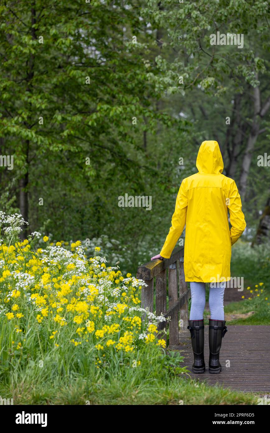 Young woman with yellow raincoat and rubber boots in spring nature ...