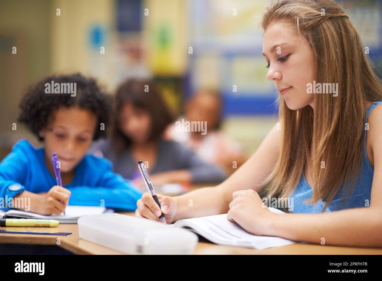 Working hard in class. A young girl working on her schoolwork in class ...