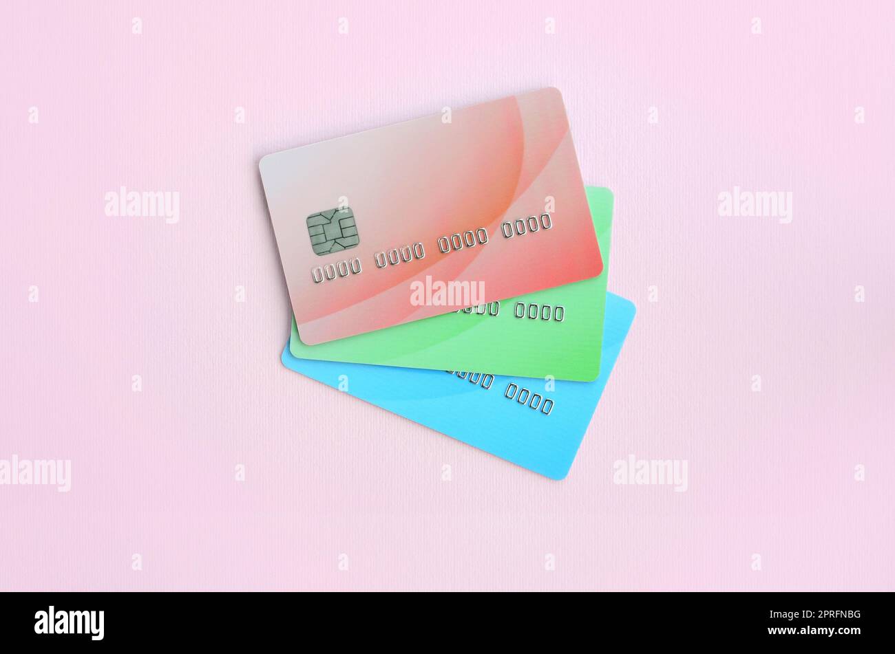 Three colored credit cards lay on a pastel pink background. The concept ...