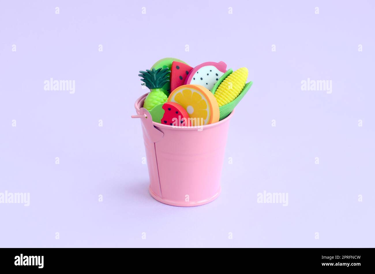 Various fresh fruits in a small pink pail on violet background ...