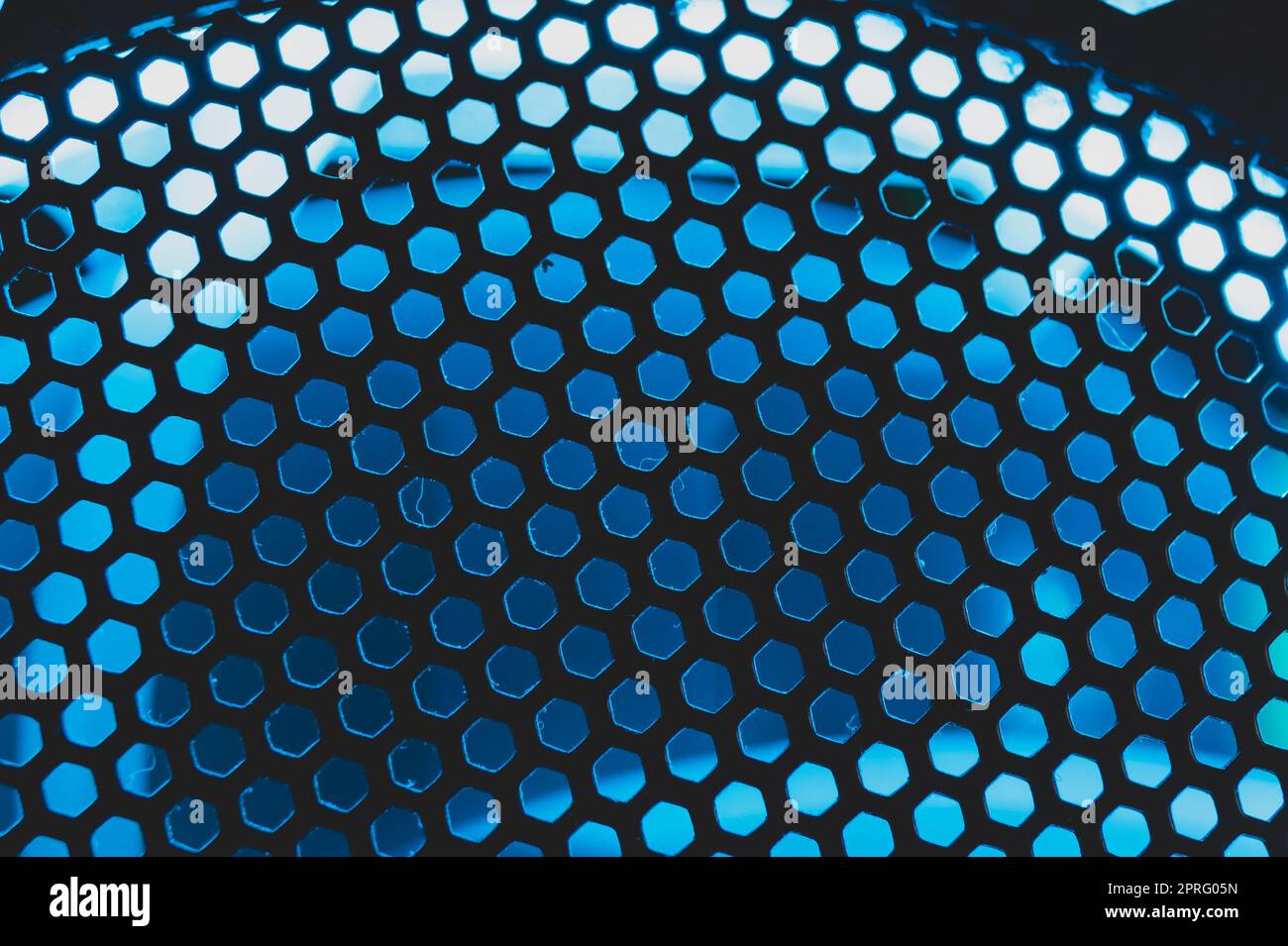 Blue light shines through the ventilation grid holes of computer air ...