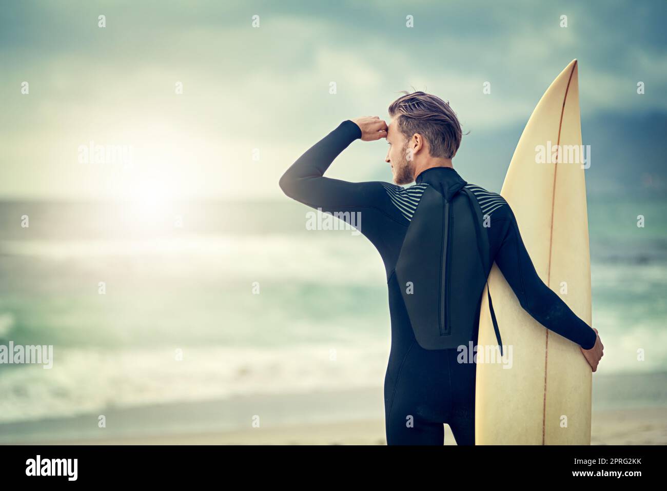 Scanning the sea for a perfect break. a laid-back young surfer watching ...