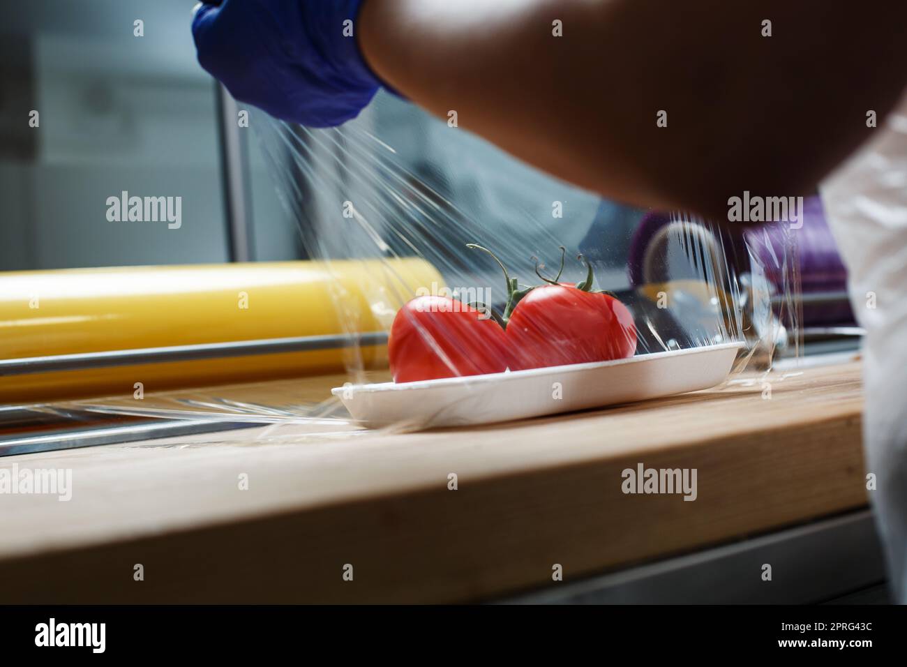 Unknown worker wraps in food transparent film tomatoes lying on white ...