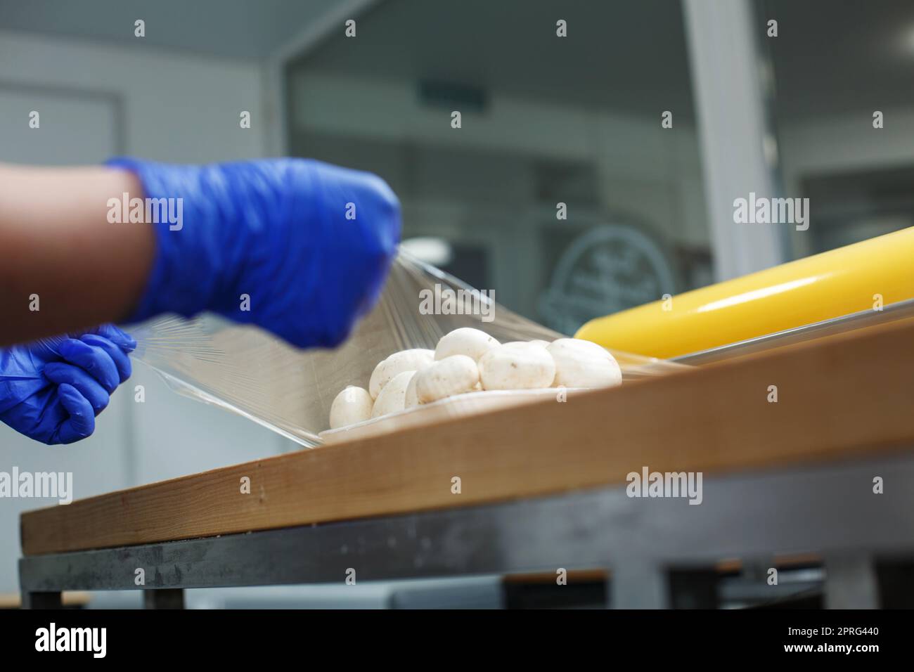 Worker wraps mushrooms lying in foam dish in stretch film Stock Photo ...
