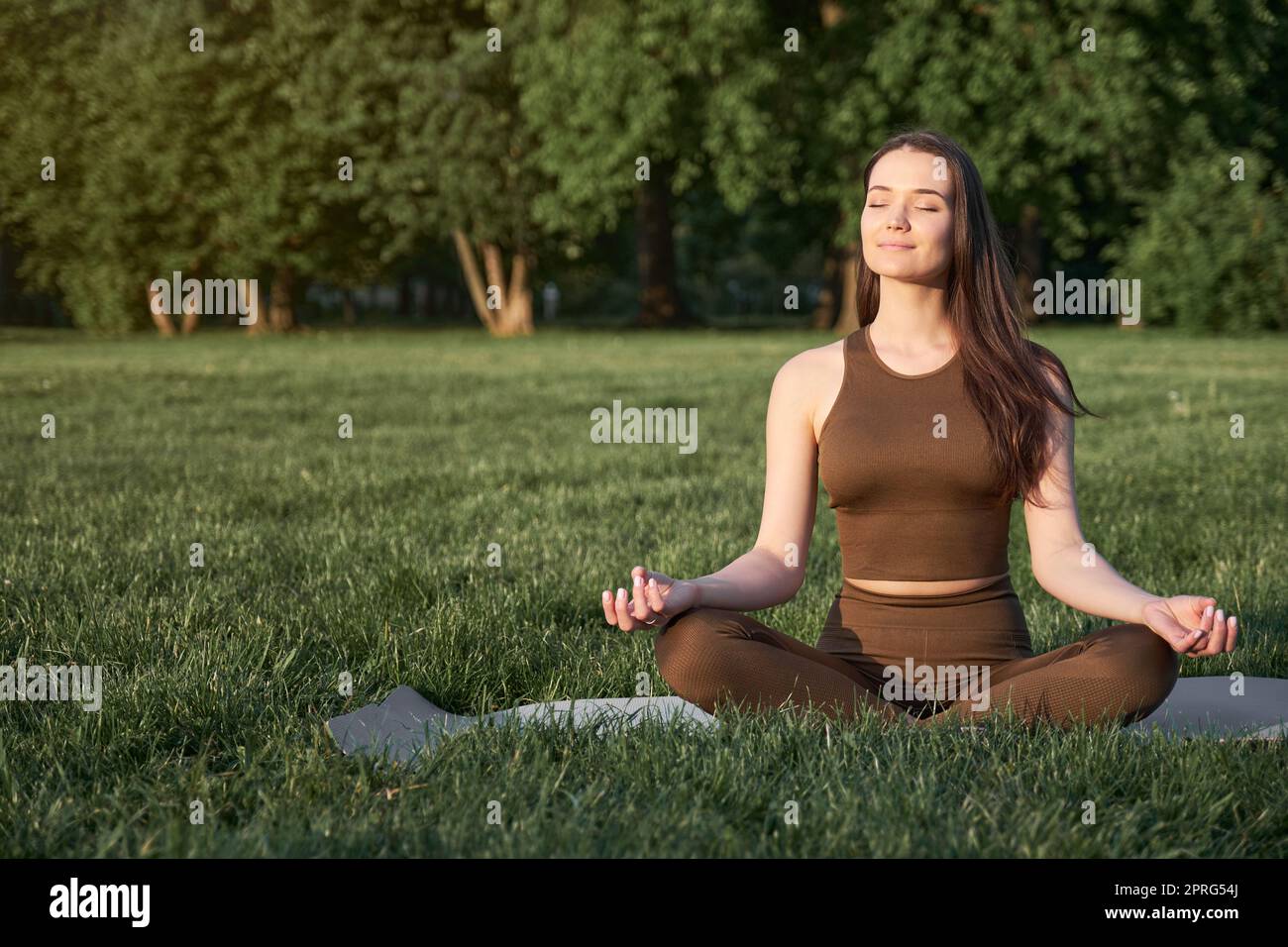 Young woman in lotus pose sitting on green grass. Concept of calm and ...