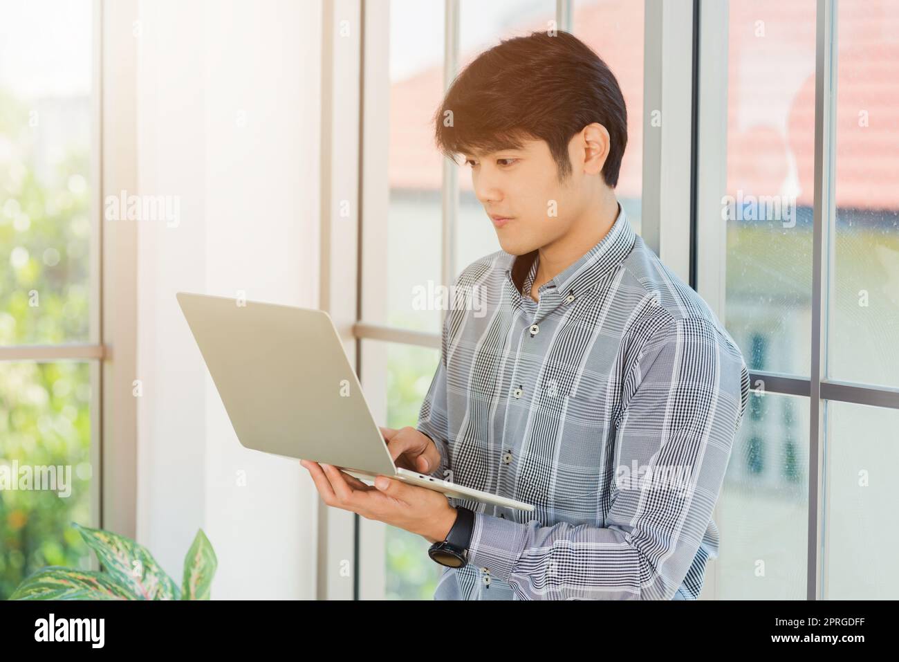 businessman smiling and working on a laptop computer stand near window ...