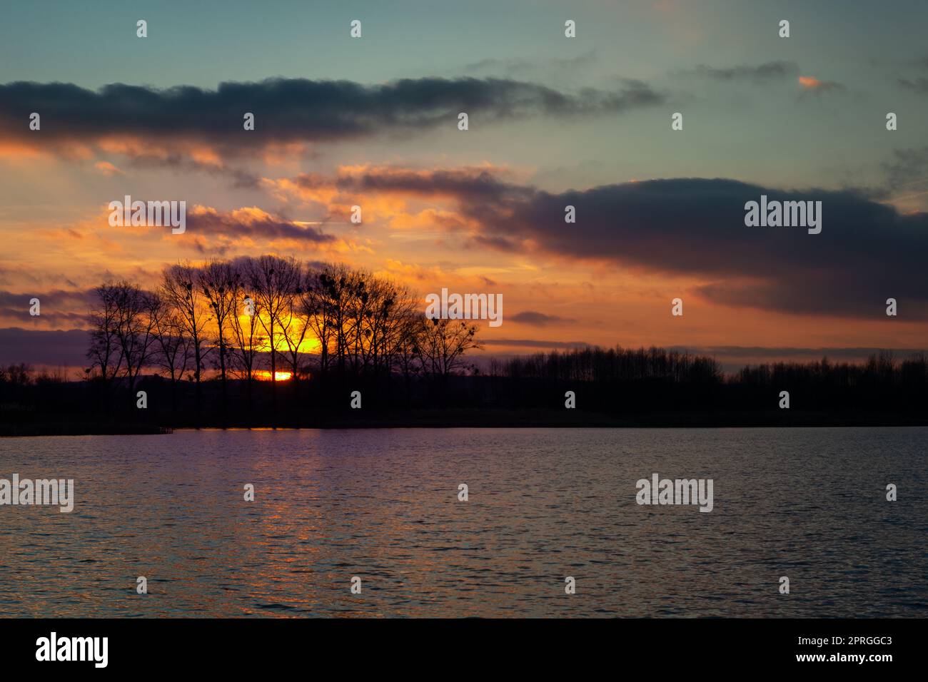 Colorful sunset and clouds behind the trees on the lake Stock Photo - Alamy