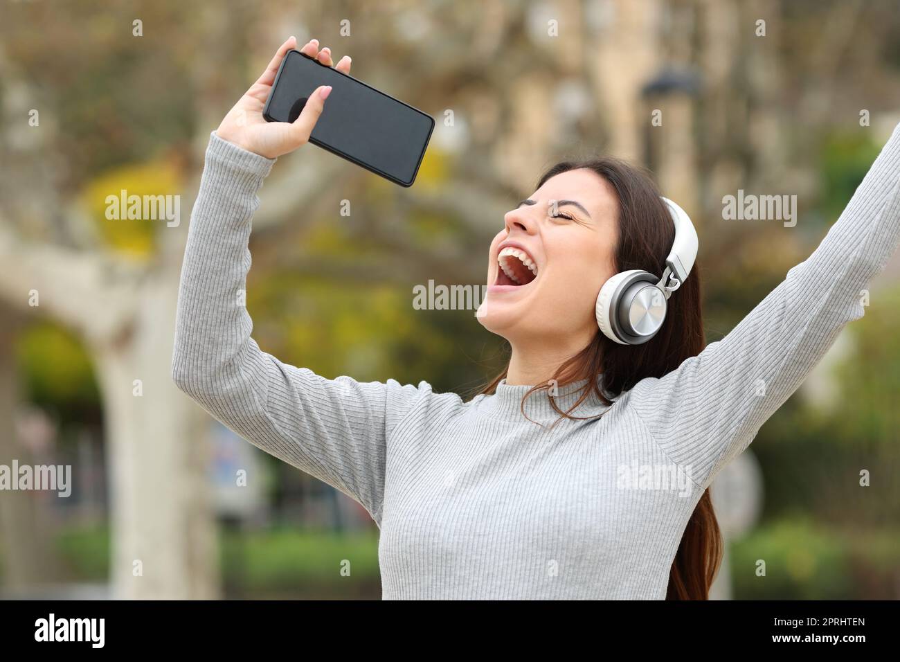 Happy teen singing listening to music showing smart phone screen in a ...