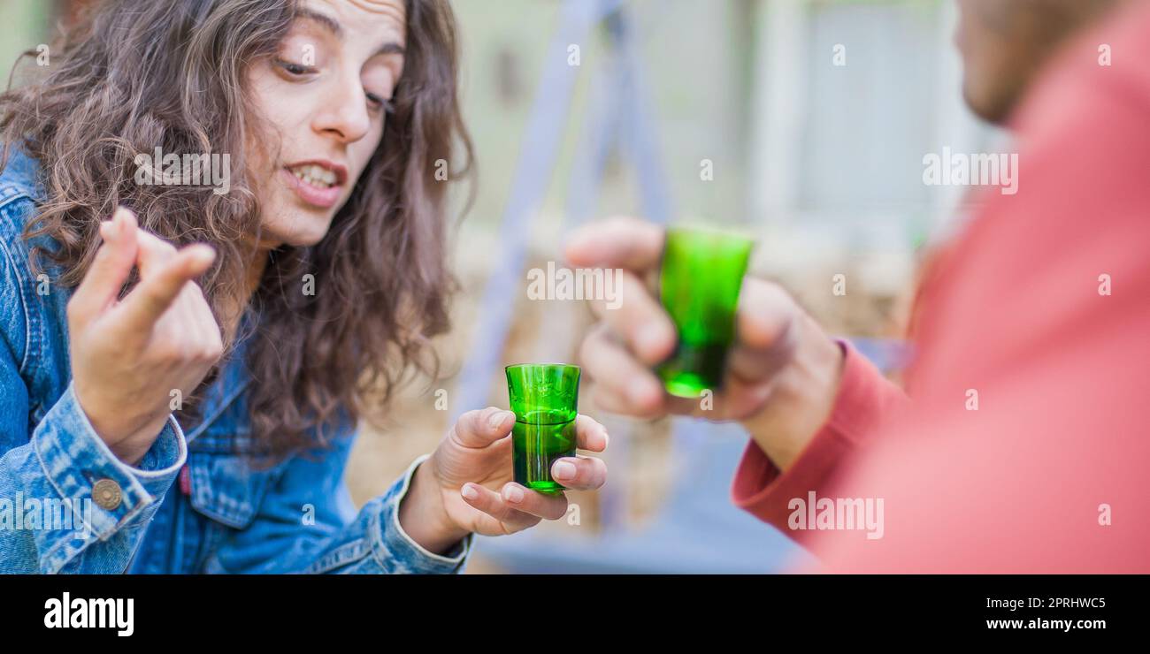 Very drunk couple, a boy and a girl, drink a strong alcoholic shot drink from small glasses. Bad ...