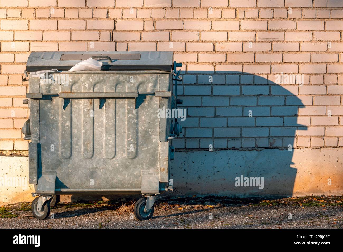 Metal container for garbage placed near white brick wall Stock Photo ...